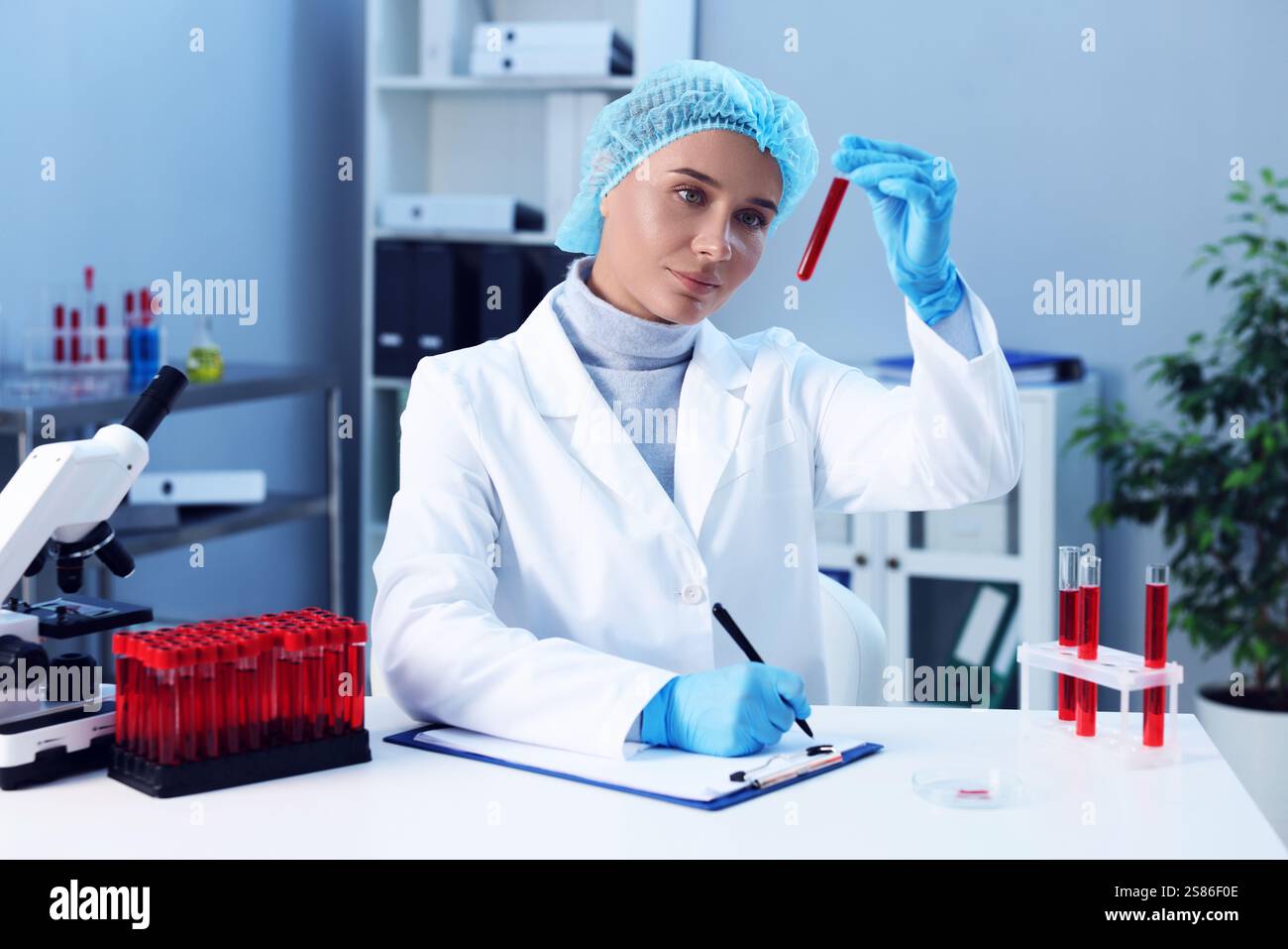 Laboratory testing. Doctor with blood sample taking notes at table ...