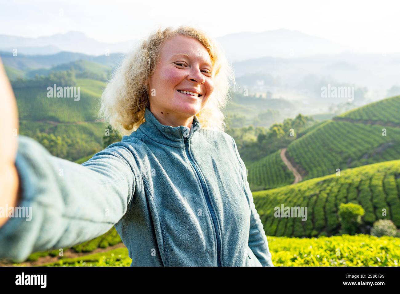Young blonde woman taking selfie with tea plantations in Munnar. Eco ...