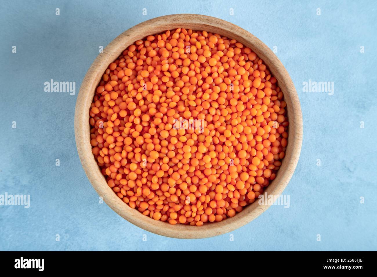 Red lentil grains in a wooden bowl on light blue background. Top view ...
