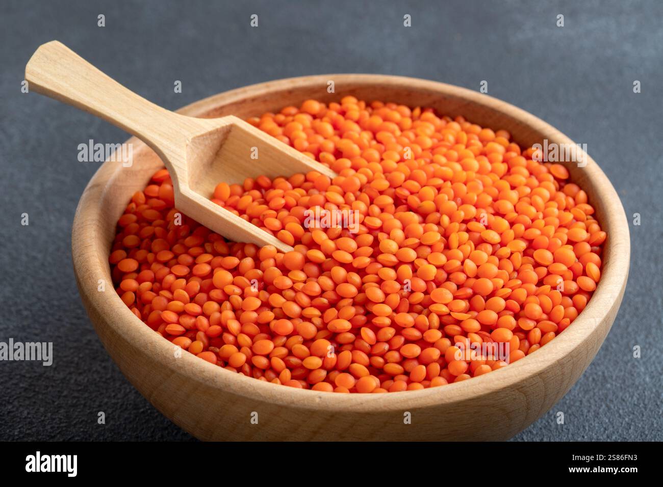 Red lentil grains in a wooden bowl and spoon on a gray background. Top ...