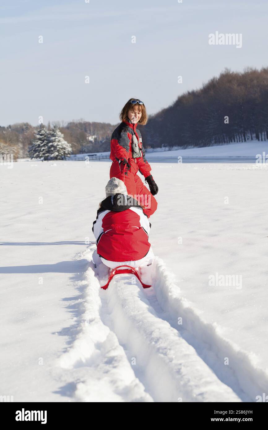 Middle aged woman pulling red sledge with her daughter across a snow ...
