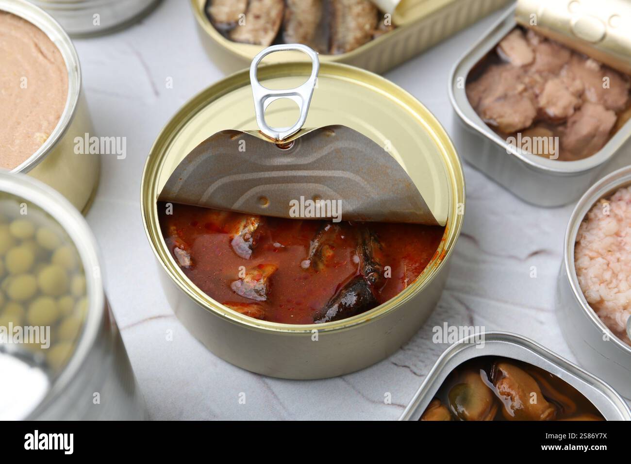 Open tin cans with different preserved products on white table, closeup ...
