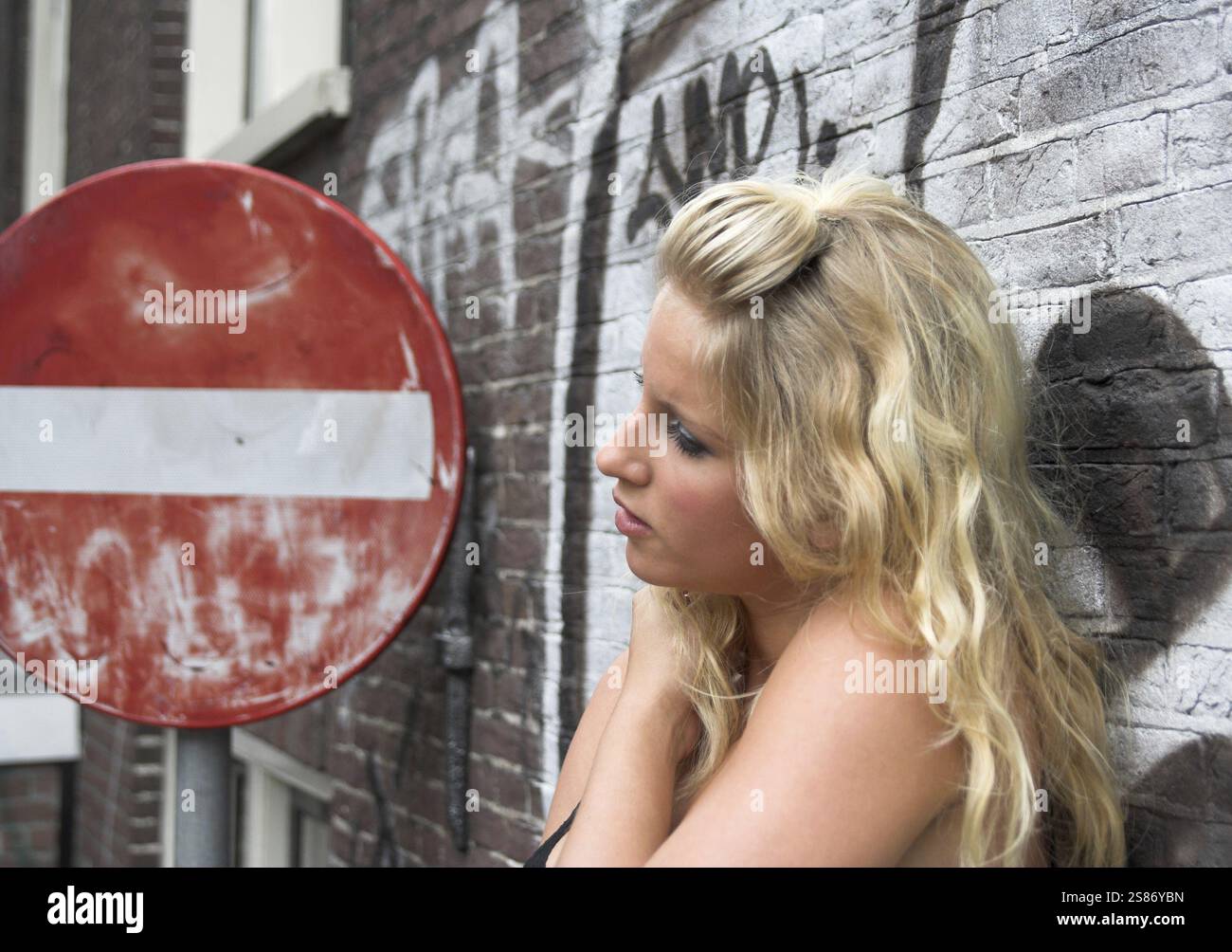 Attractive blonde against a brick wall with graffiti, standing next to ...