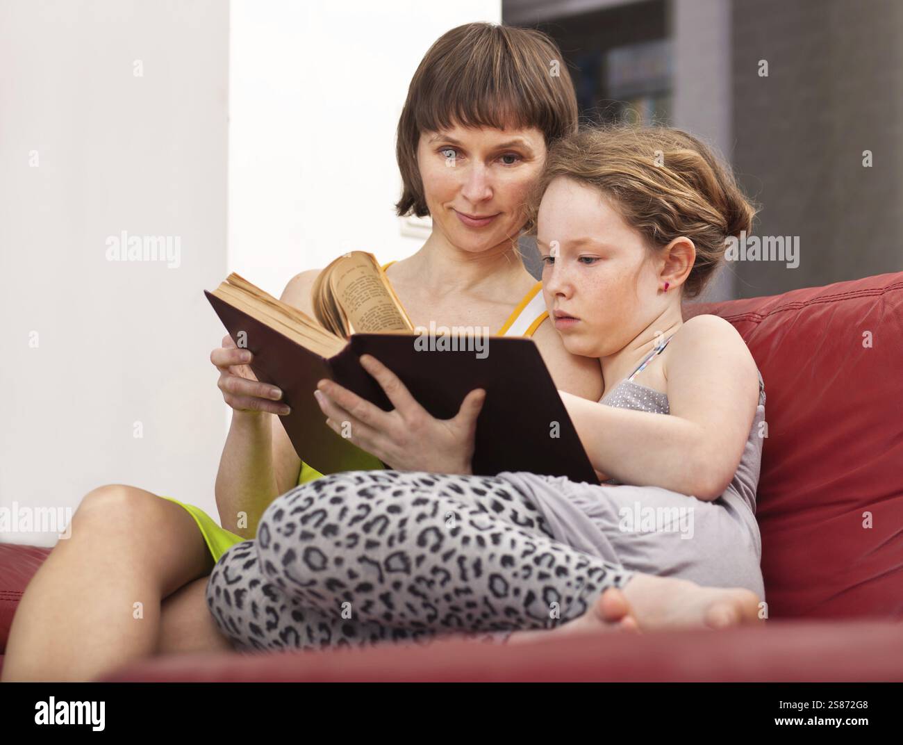 Teenager girl and her mother sitting on sofa and reading book together, Belgium, Europe Stock ...