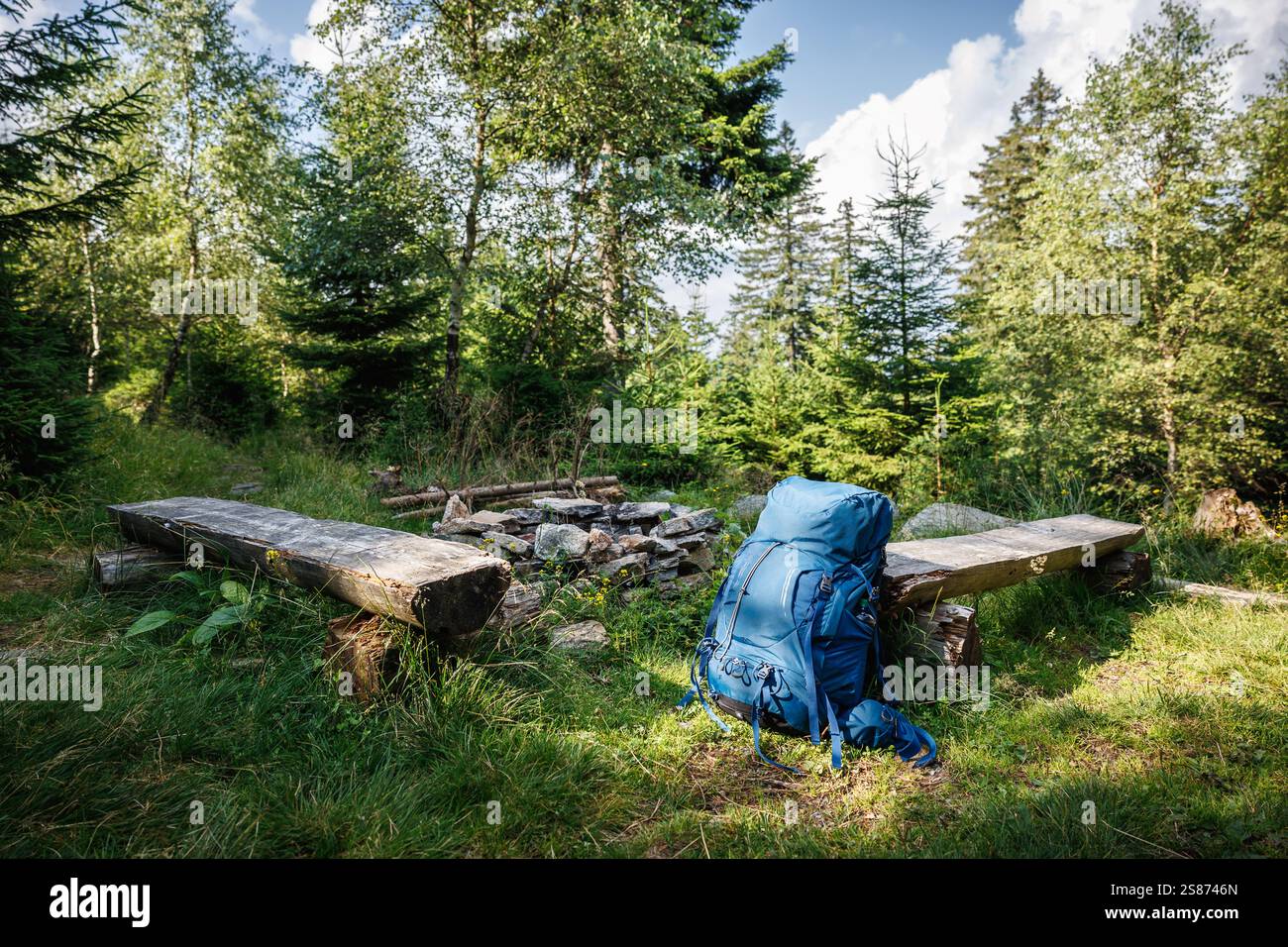 Camping area with campfire in the forest. Hiking backpack at wooden ...