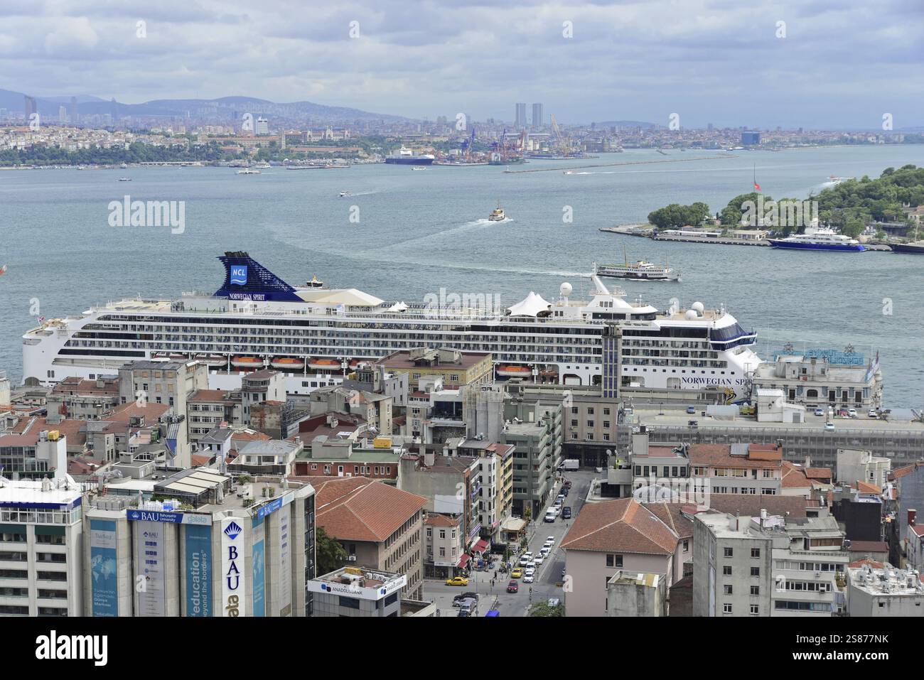 A large cruise ship in the harbour of a densely built city under clouds ...
