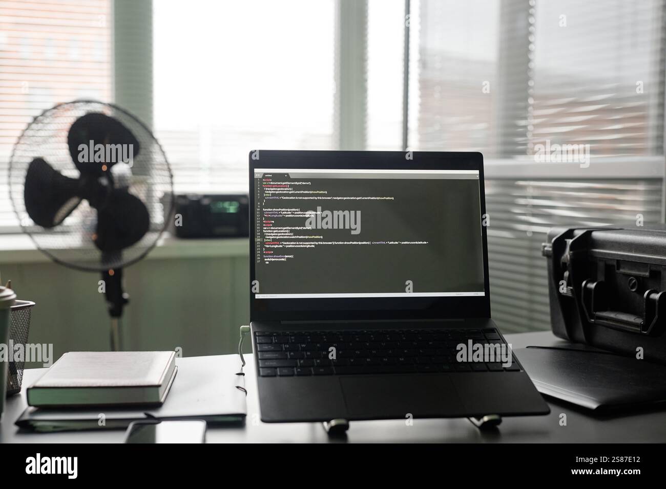 Background shot of laptop on support stand placed on professional programmers desk with various ...