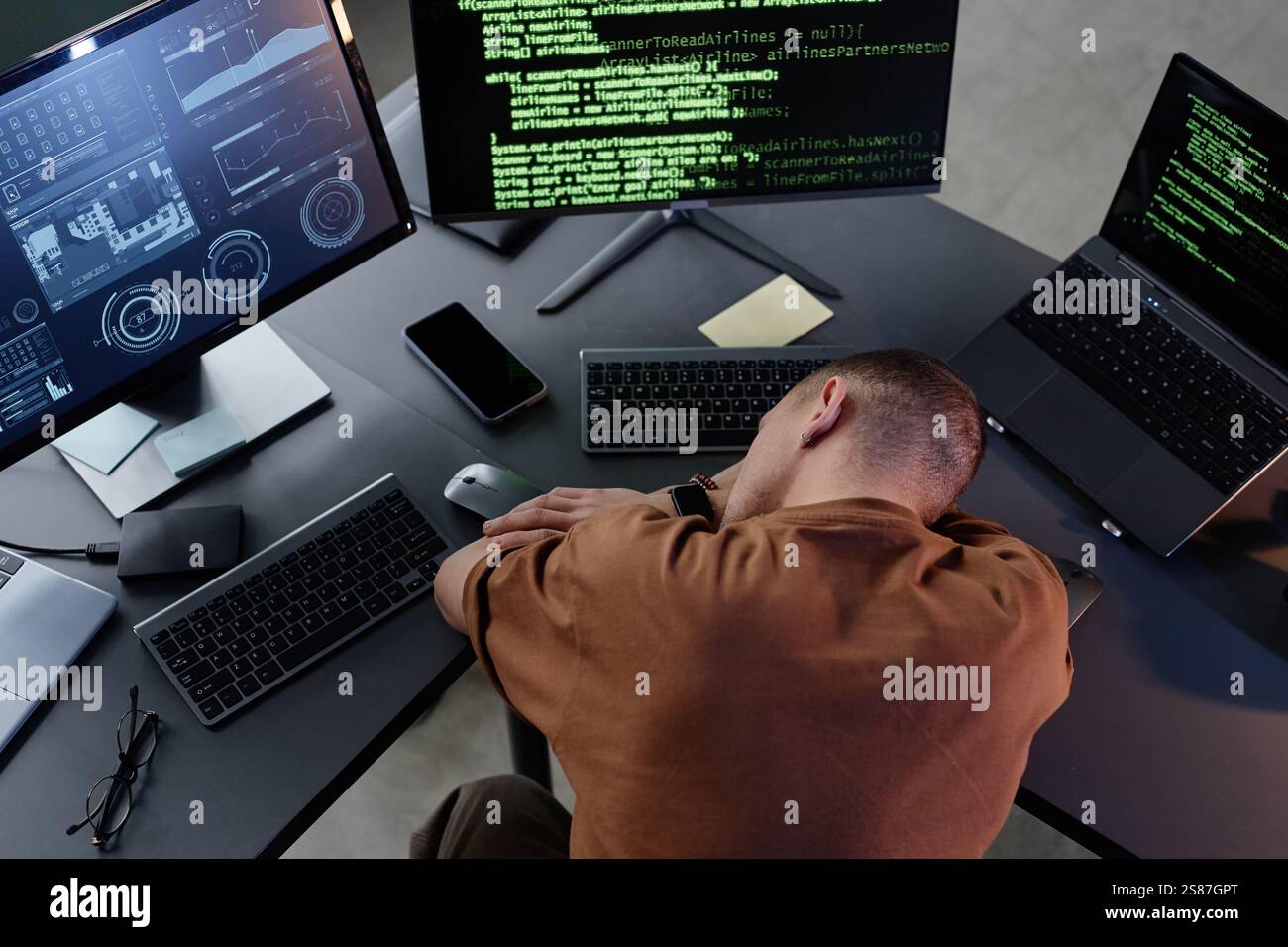 Top view of exhausted male programmer lying on desktop with several ...