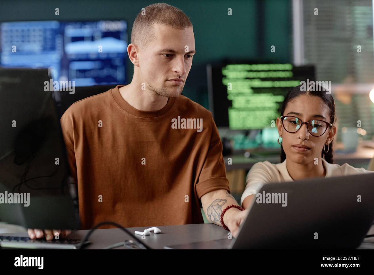 Medium shot of male senior IT programmer reviewing code on colleagues laptop while working ...