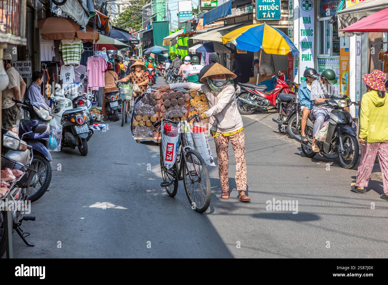 A Vietnamese lady pushing a heavily loaded bicycle down a busy street ...