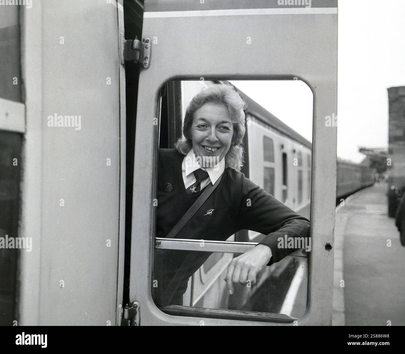 1987, female British Rail ticket collector leaning for a photo out of a ...