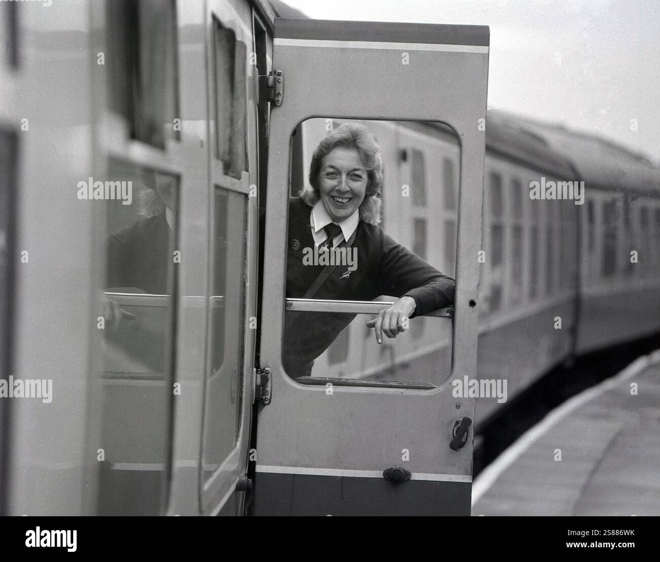1987, on a platform, a female British Rail ticket collector leaning for ...