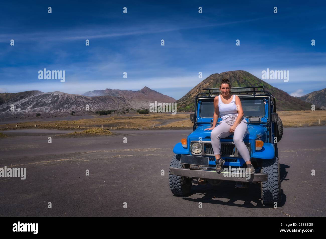 A confident woman poses on a striking blue jeep, set against a stunning ...