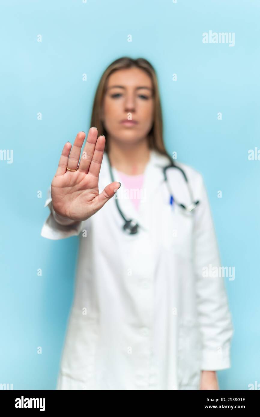 vertical Young female doctor with stethoscope showing stop sign with ...
