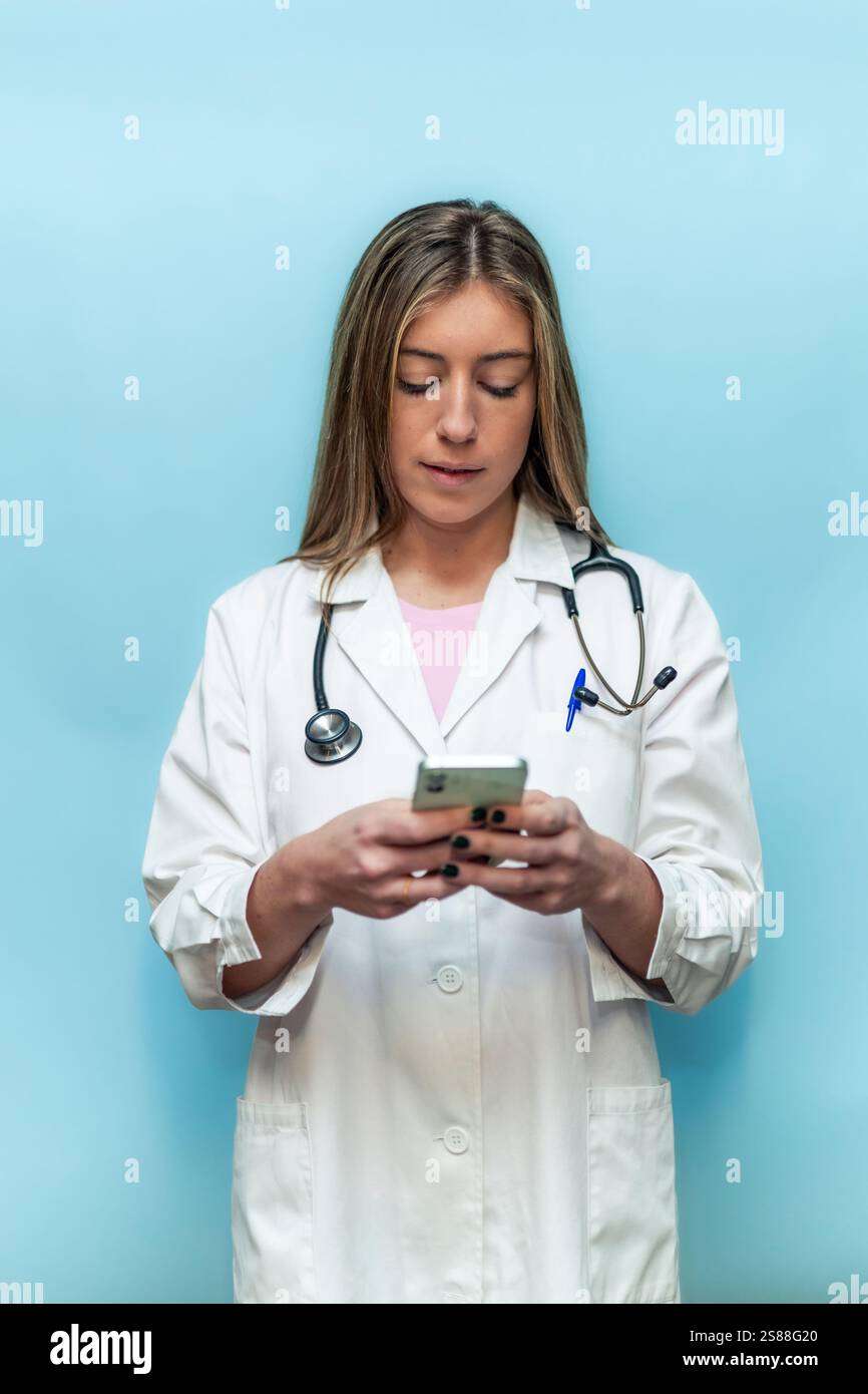 vertical Young female doctor wearing white coat and stethoscope, using ...