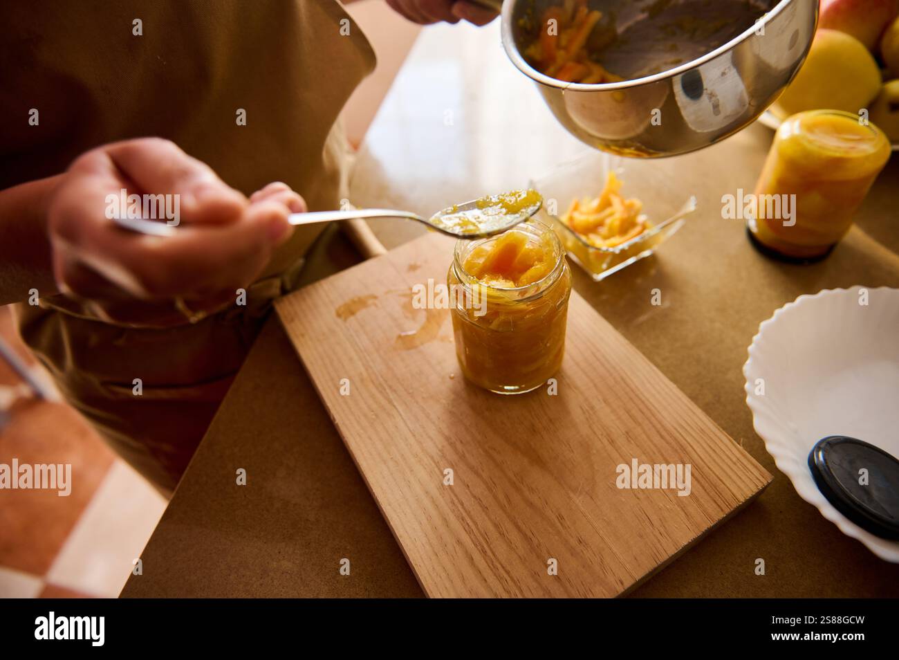 A close-up of a person using a spoon to prepare fruit jam in jars ...