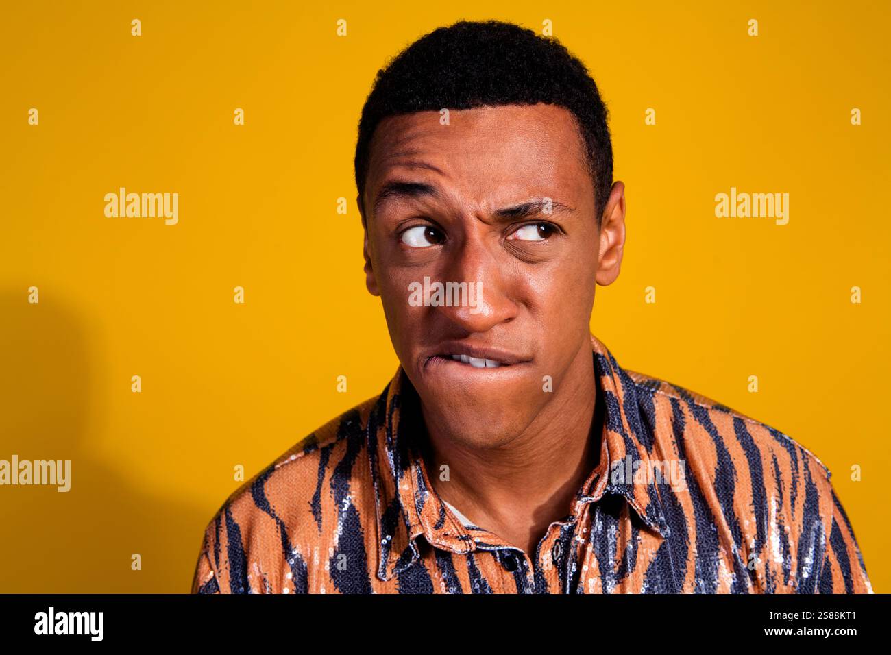 Stylish young man biting lip wearing animal print shirt posing against ...