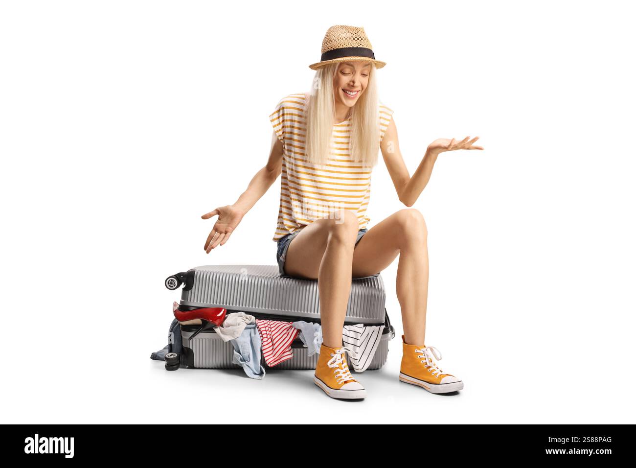Funny young woman sitting on an overpacked suitcase and laughing ...