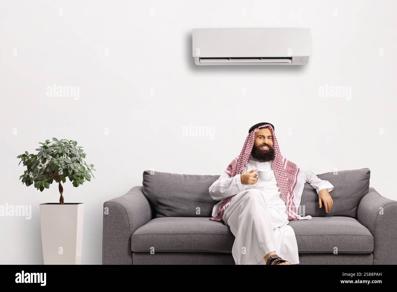 Saudi arab man sitting on a sofa with a cup of tea under an air ...