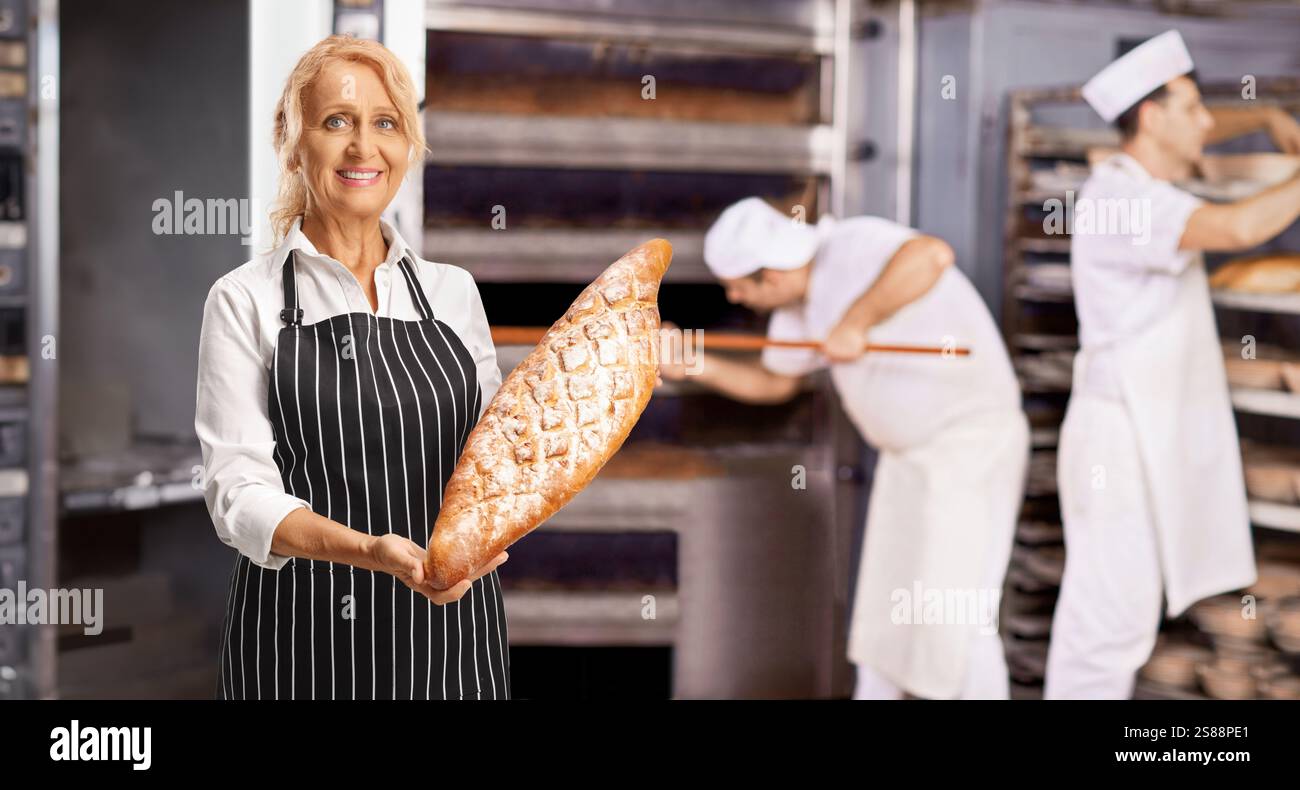Woman baker holding a loaf of bread in front of ovens in a bakery Stock ...
