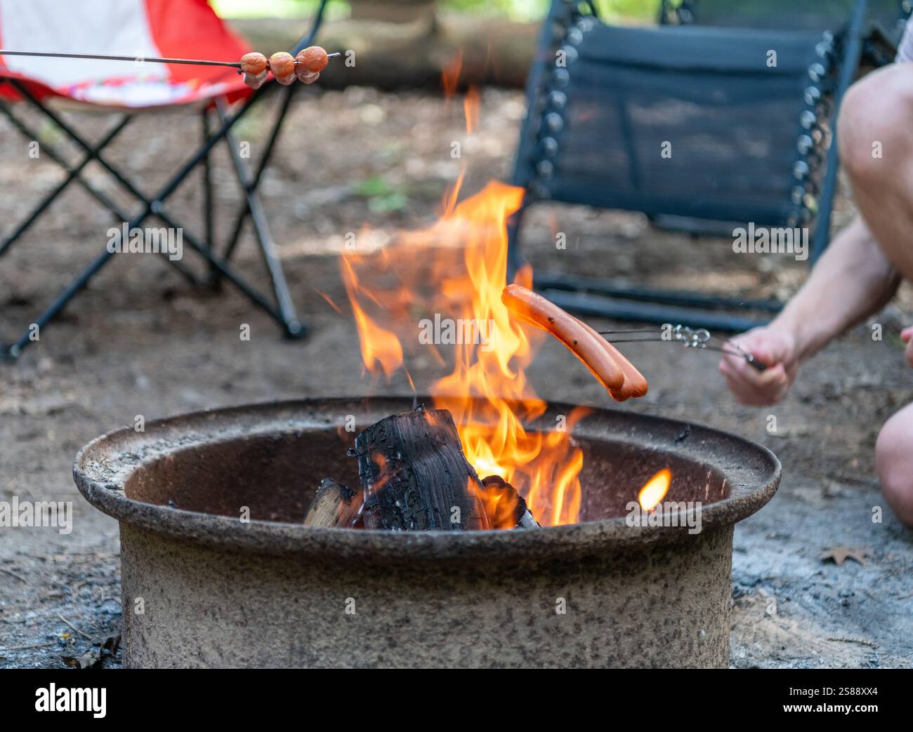 roasting hot dogs over campfire pit and grill, smoke bbq and pile of ...