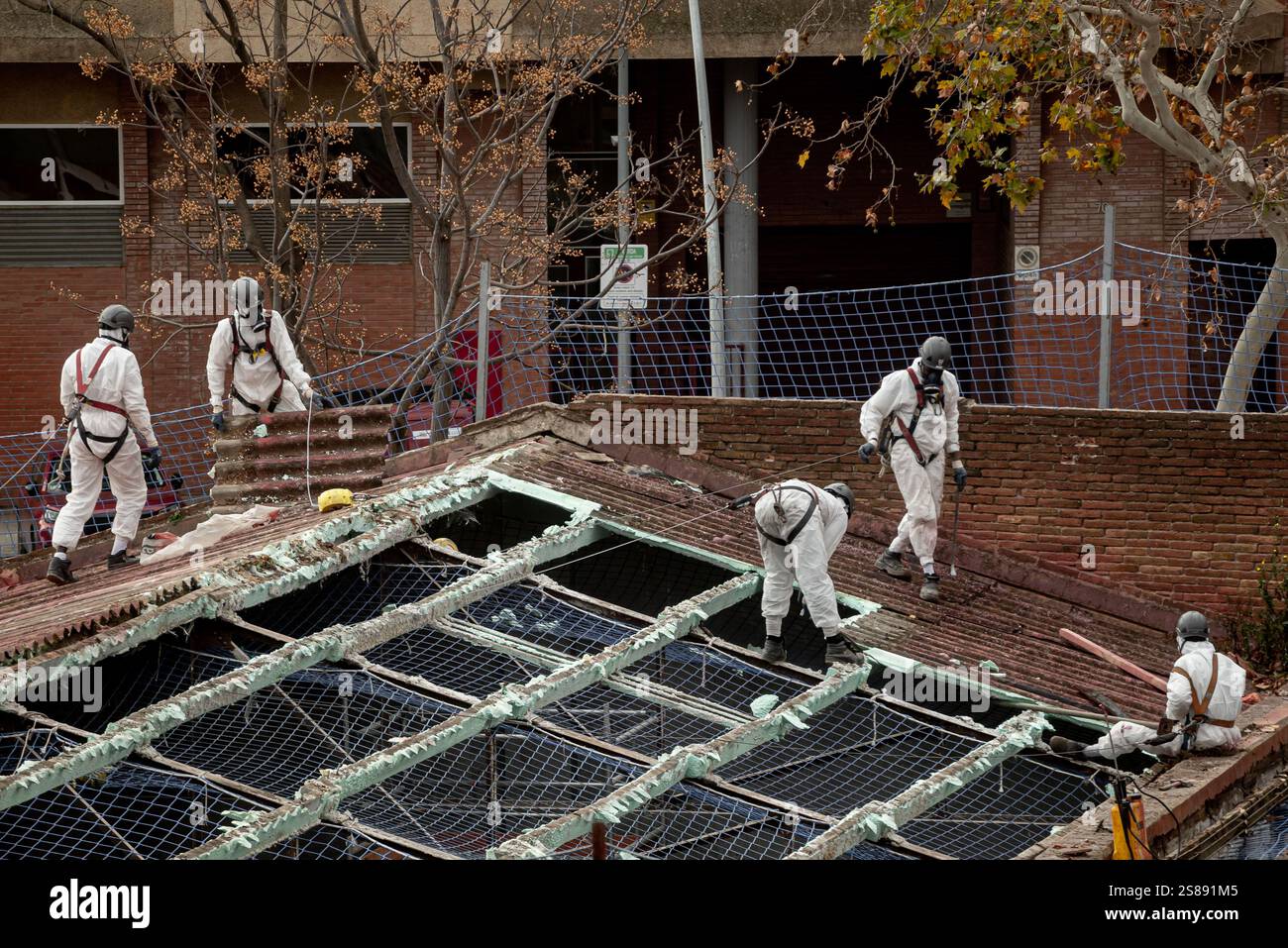 Workers in hazmat suits remove asbestos cement plates from the roof of ...