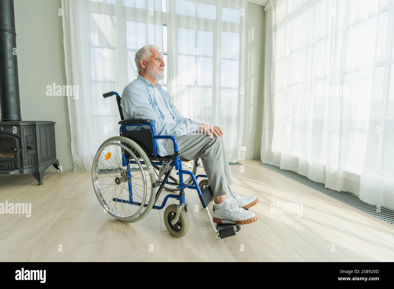 Sad senior man sitting in wheelchair looking out window in retirement ...