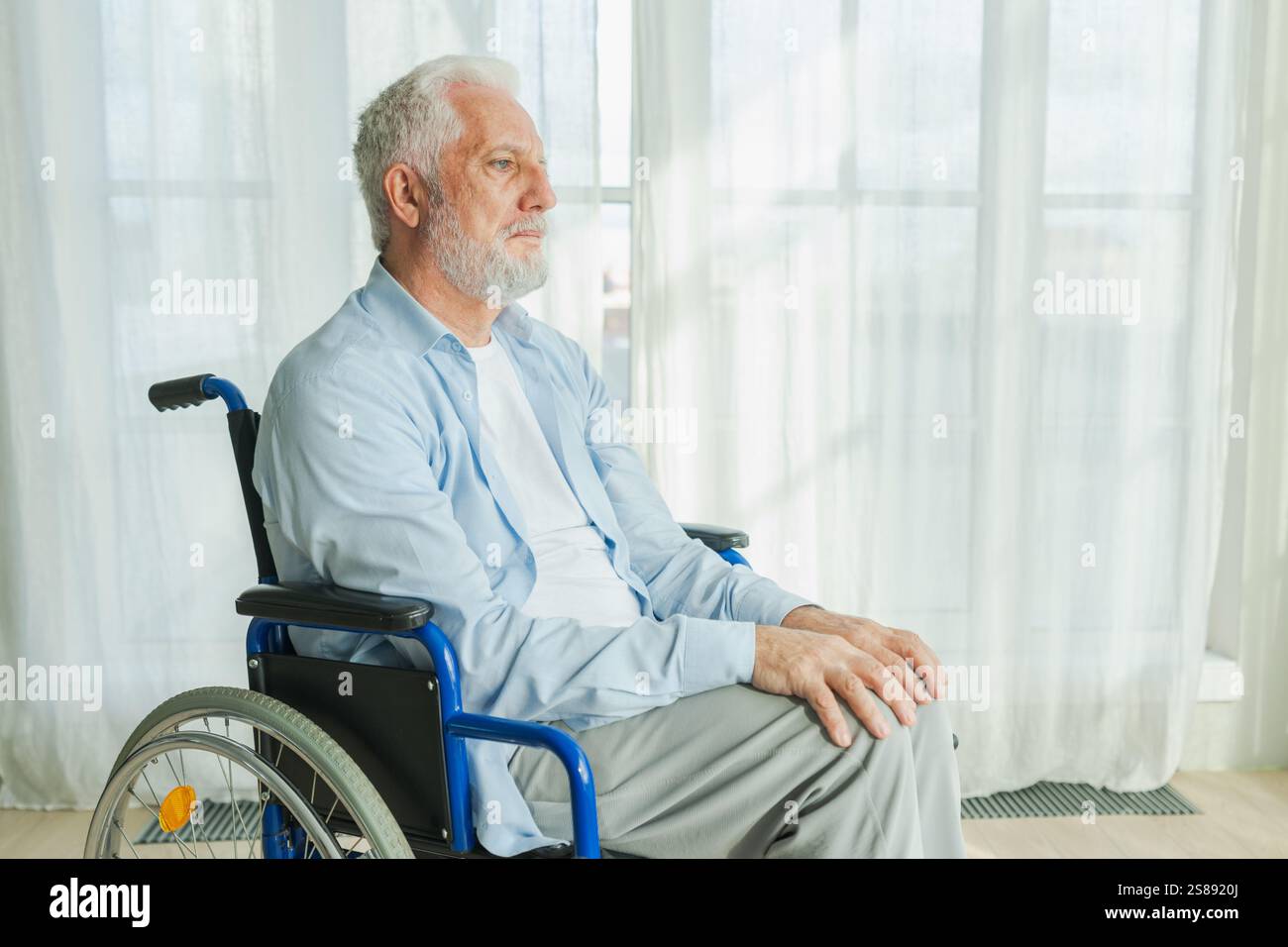 Sad senior man sitting in wheelchair looking out window in retirement ...