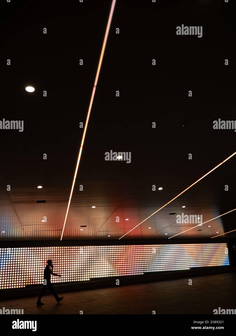 Pedestrian walks past lit wall at night Stock Photo - Alamy
