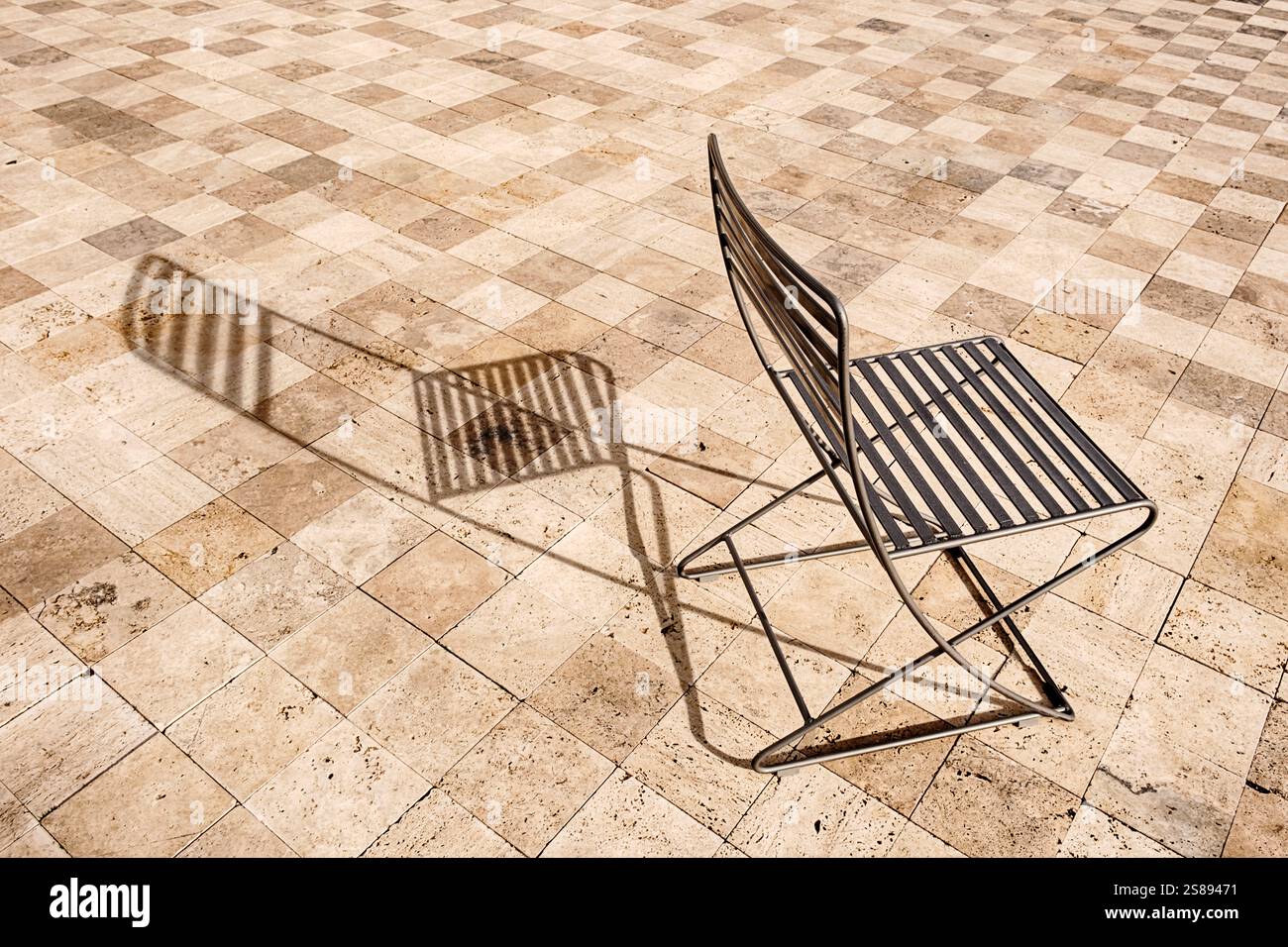 A simple metal folding chair casts a shadow from the sun on the ...