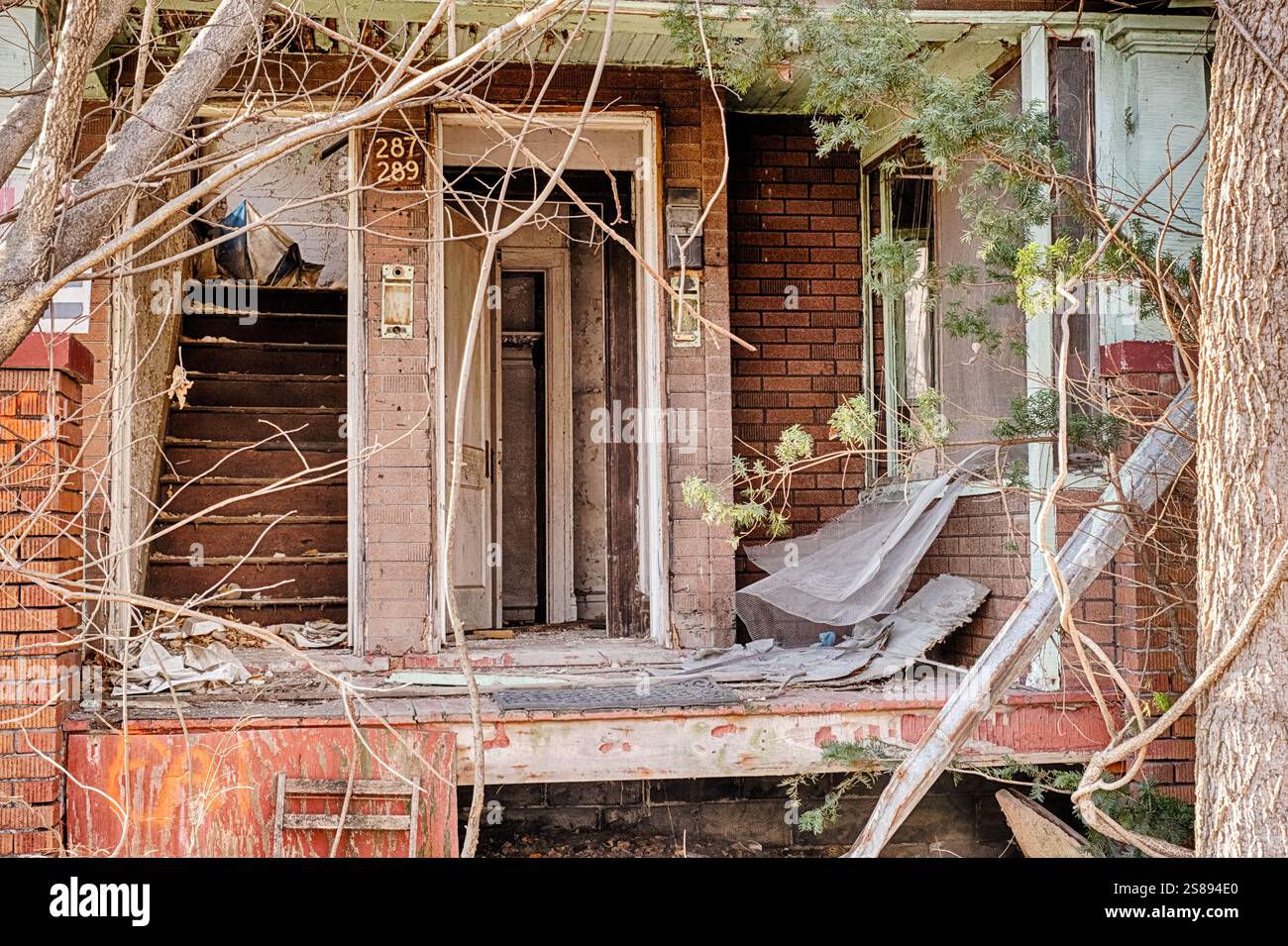 The porch of an abandoned duplex is torn apart with open doors and junk ...