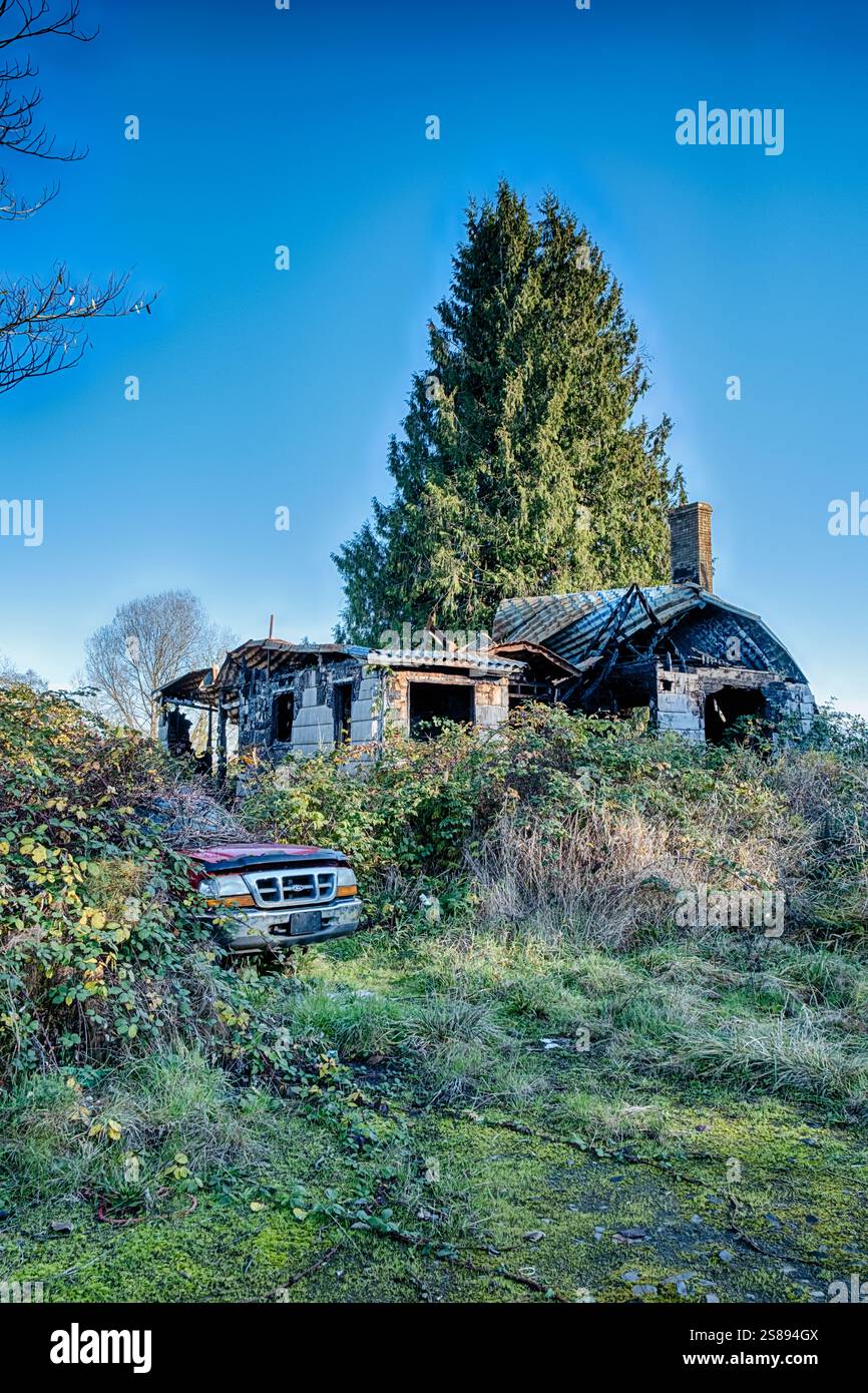 A burned out house is rotting away next to an old junked car in ...
