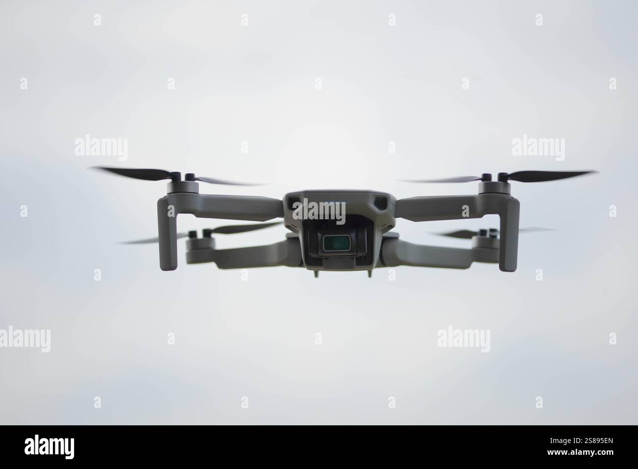 A small white drone is flying in the sky. The drone is equipped with a ...