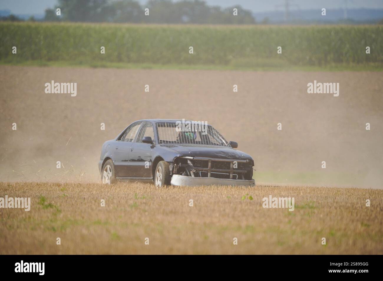 A black car is driving through a field of dry grass. The car is damaged ...