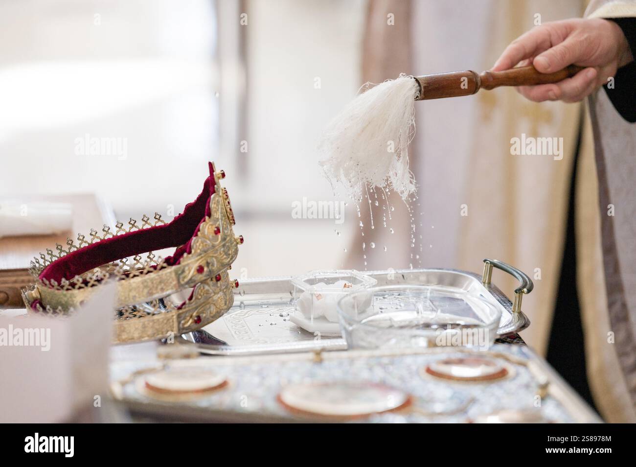 Close-up of a golden crown and a person pouring holy water during a ...