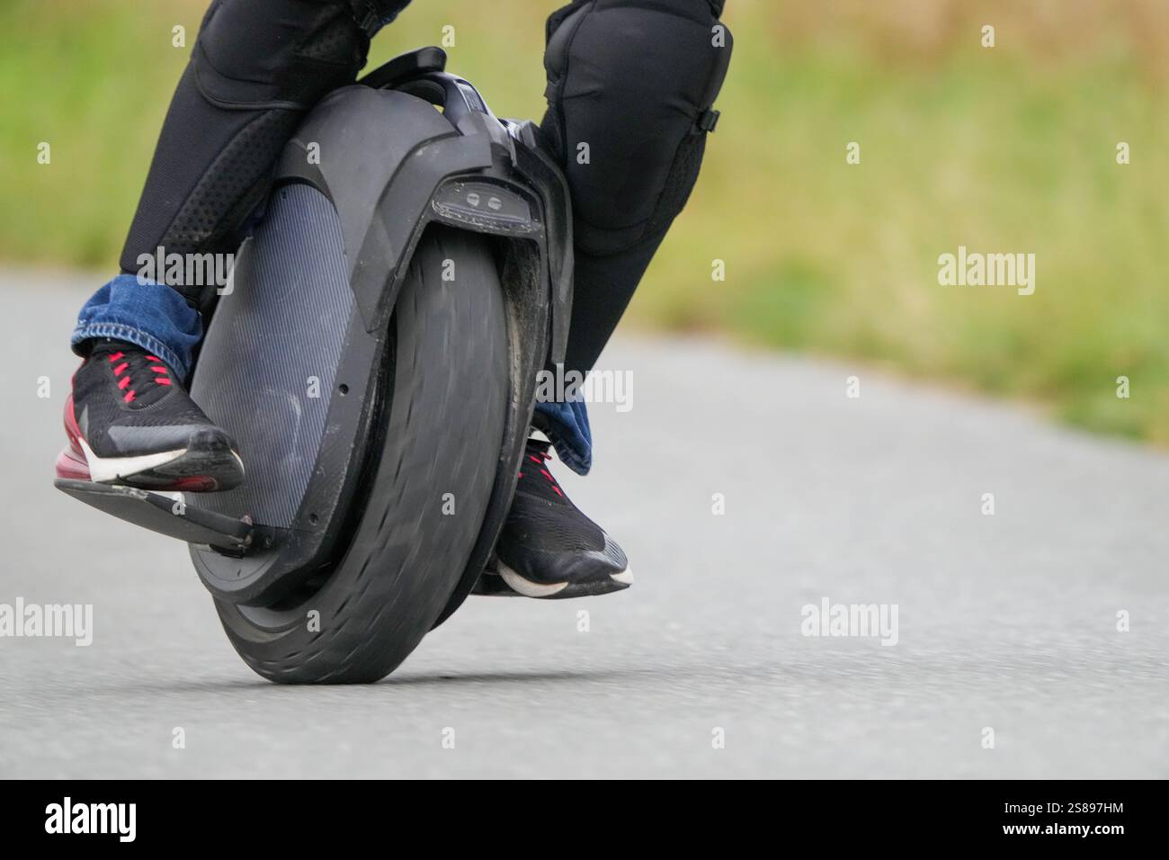 A man is riding a electric unicycle euc on a road. The sky is blue and ...