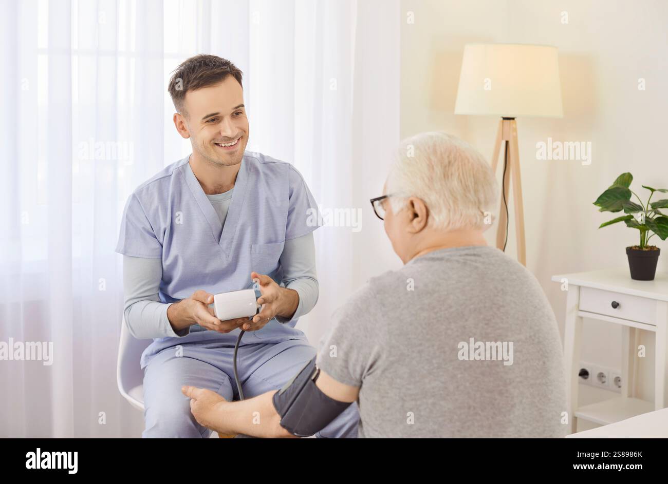 Caregiver smiling while measuring blood pressure of senior patient ...