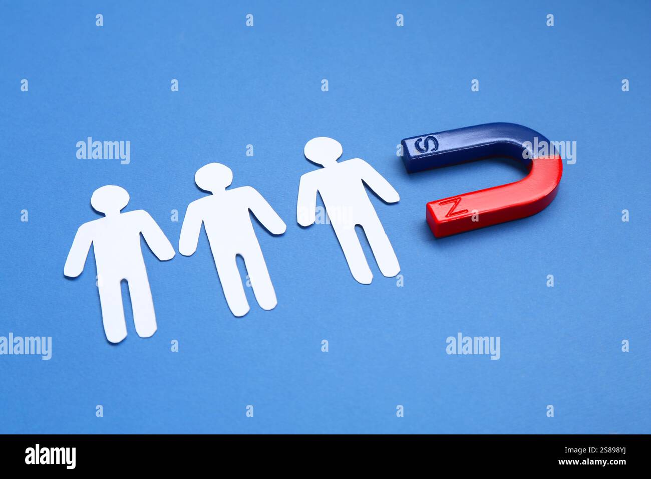 Magnet attracting paper human figures on blue background Stock Photo ...