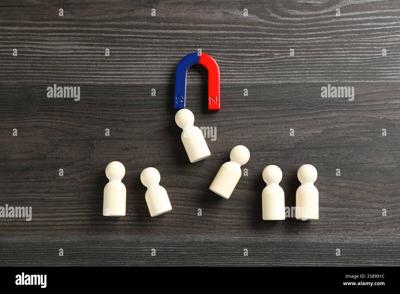 Magnet attracting human figures on wooden table, flat lay Stock Photo ...