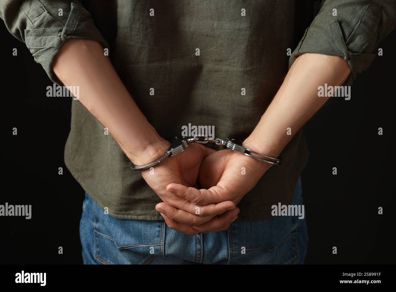 Man in metal handcuffs on black background, back view Stock Photo - Alamy