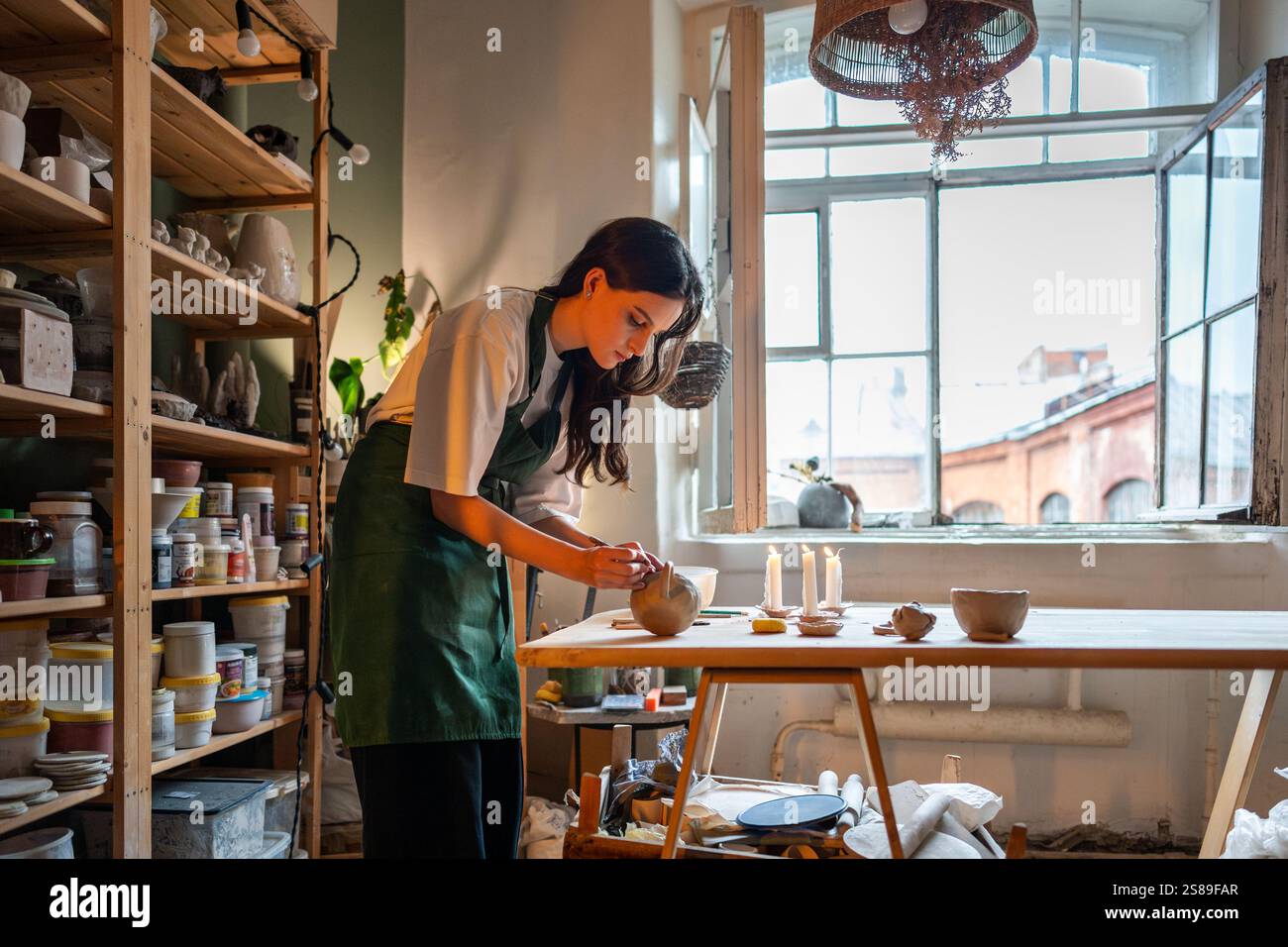 Concentrated female clay artist molding intricate designs with knife on ...