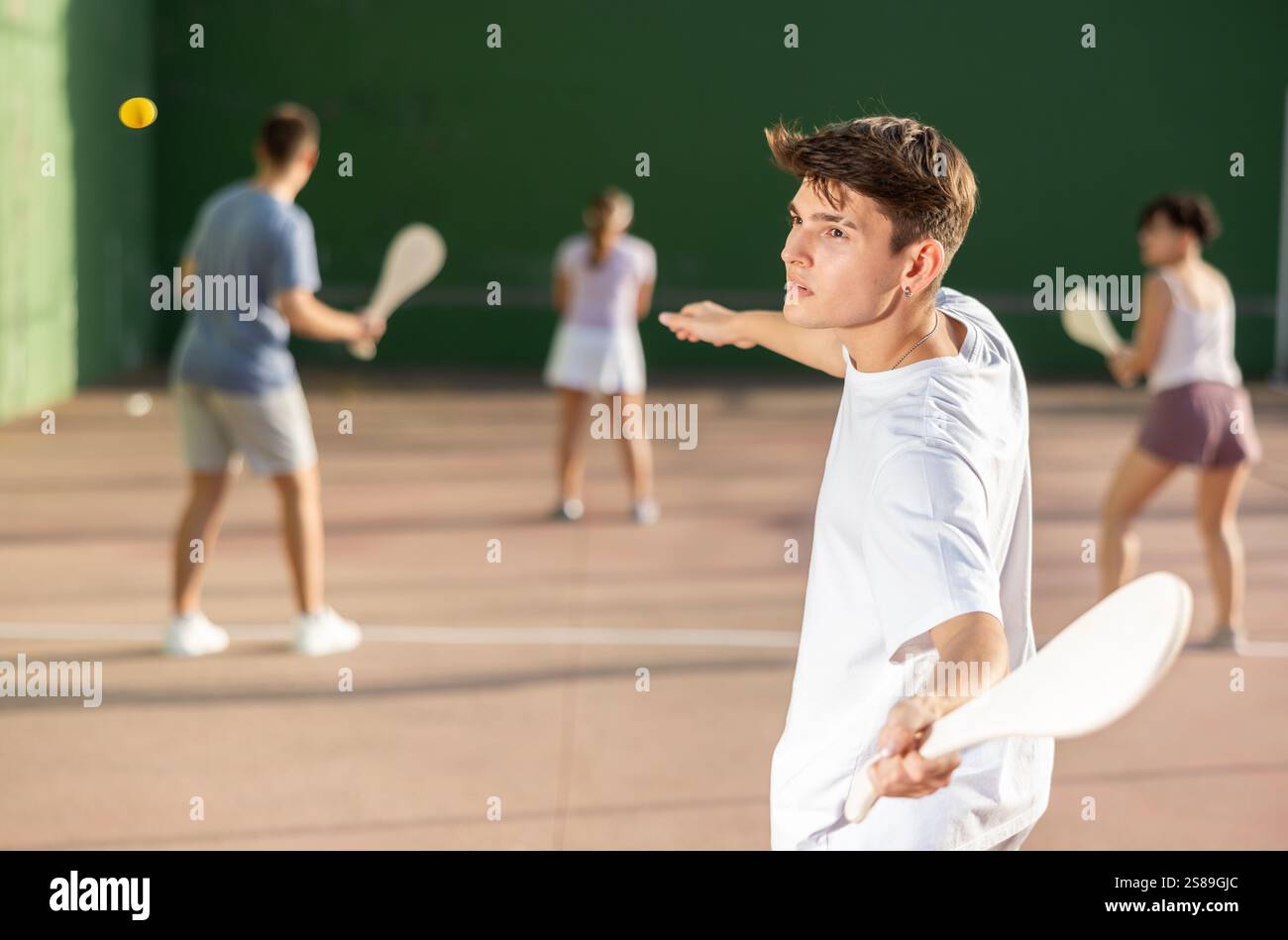 Sporty guy playing pelota with wooden racket on open fronton court ...