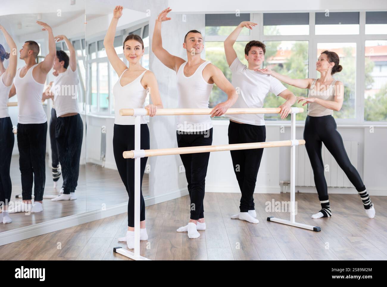 Group practicing ballet positions at barre with female instructor Stock ...
