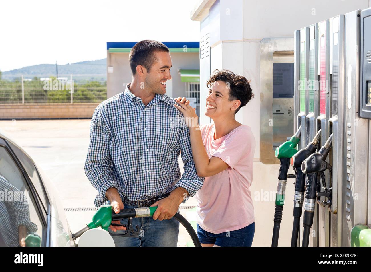 Positive couple filling up tank of their car with gasoline in gas ...