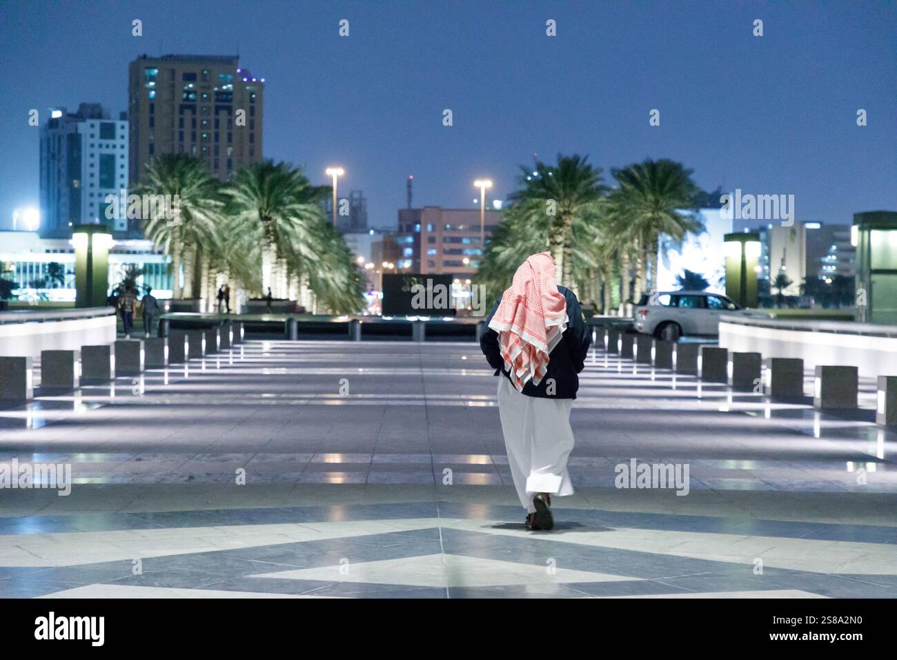 Qatar, Doha. Traditionally dressed man walking along marble walkway in ...
