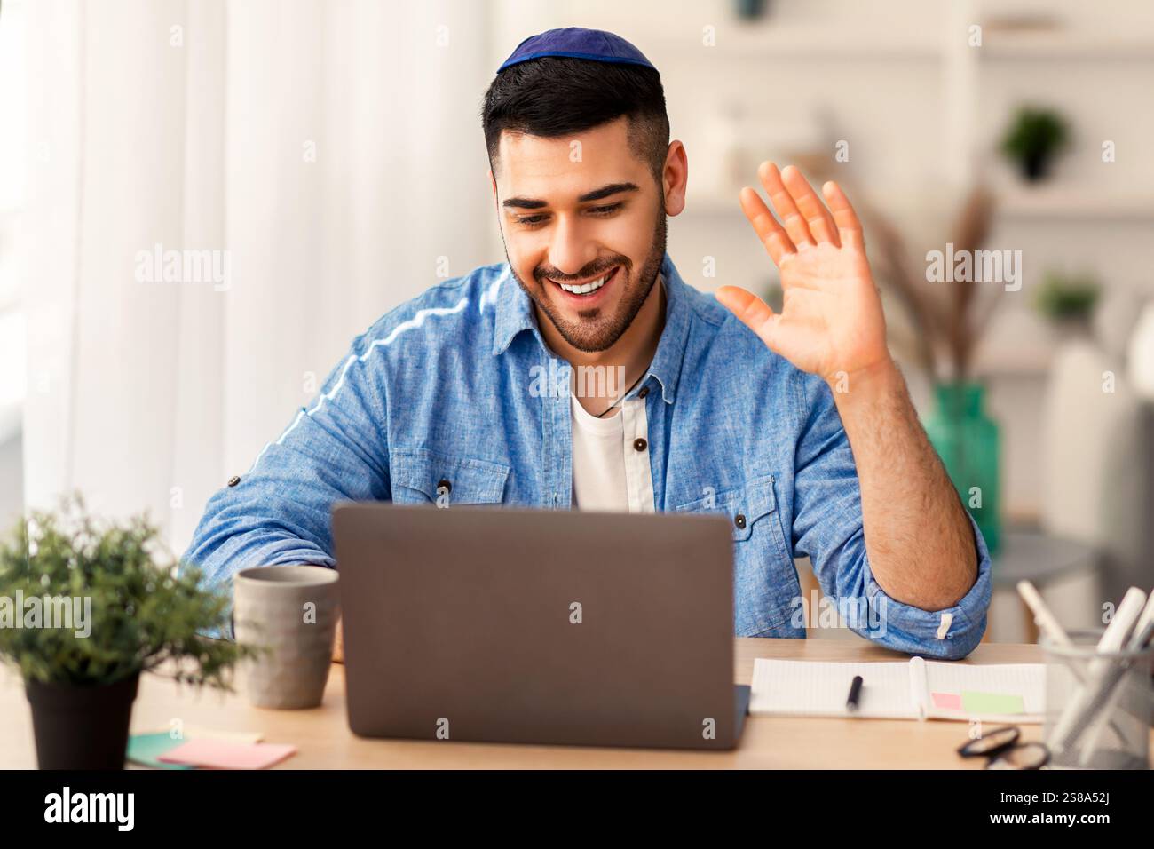 Smiling israeli man working on laptop waving hand Stock Photo - Alamy