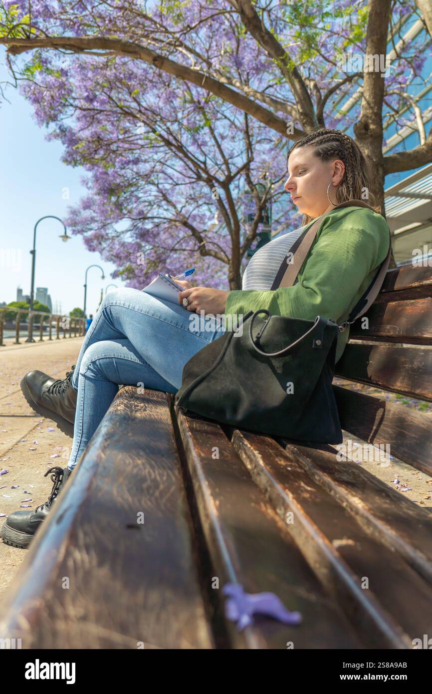 Vertical shot of a woman in a green jacket writing in a notebook while ...