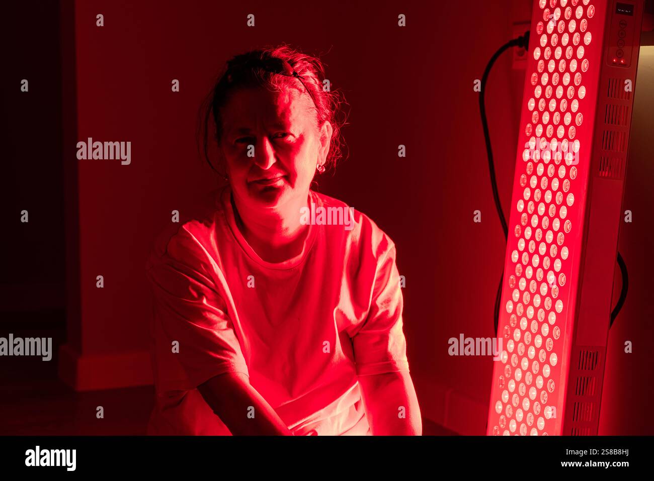 Elderly woman seated near a red light therapy panel during her therapy ...