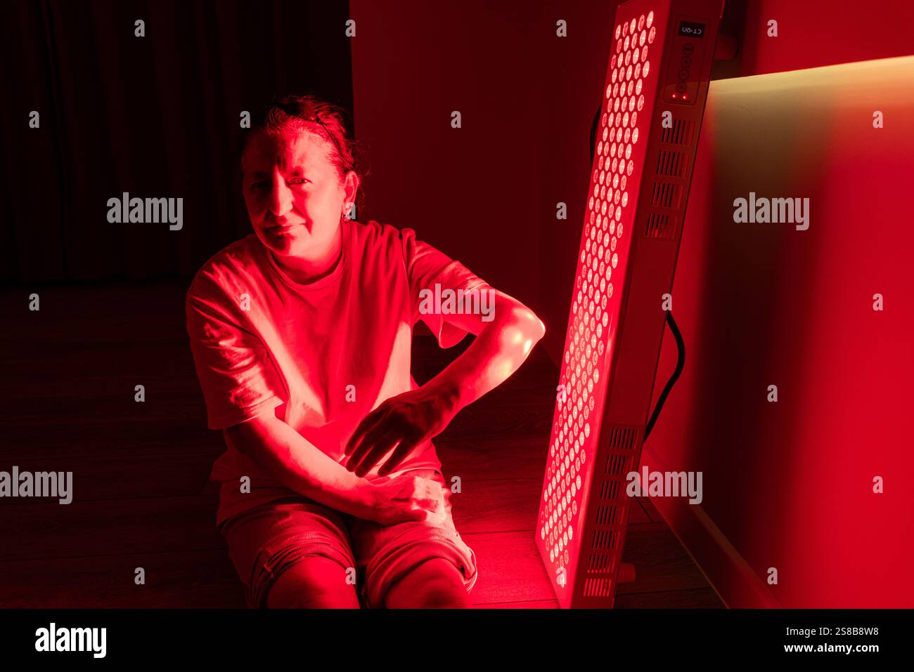 Elderly woman adjusting the position of her arm under red light therapy ...