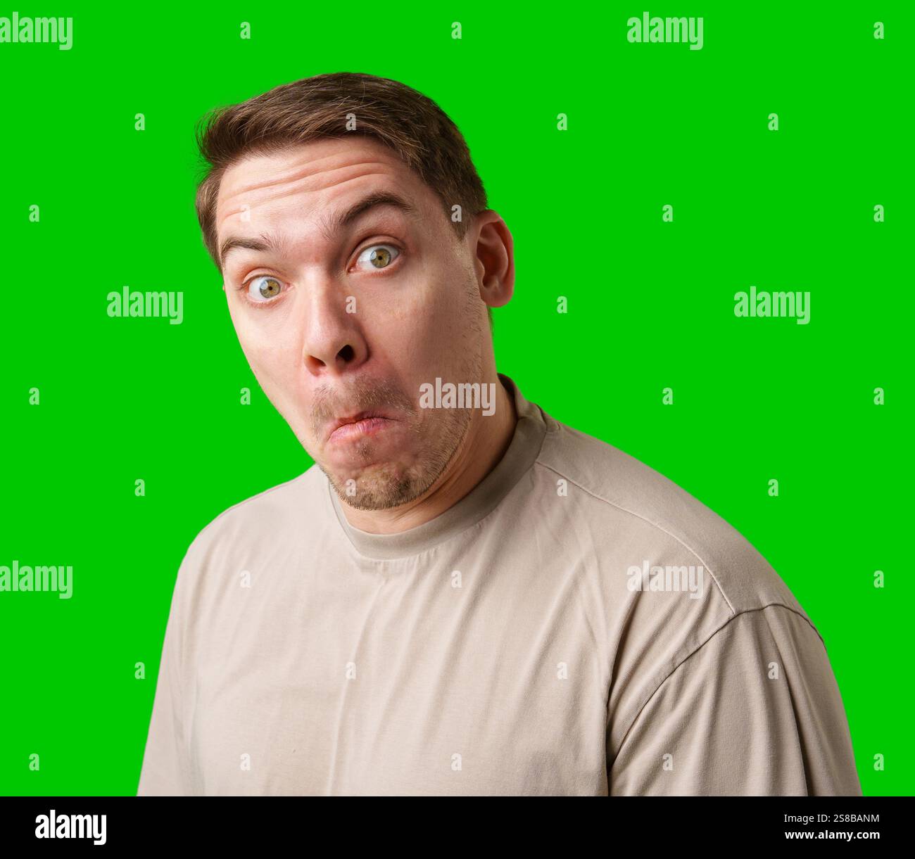 A surprised man stands in front of a bright green screen, expressing ...